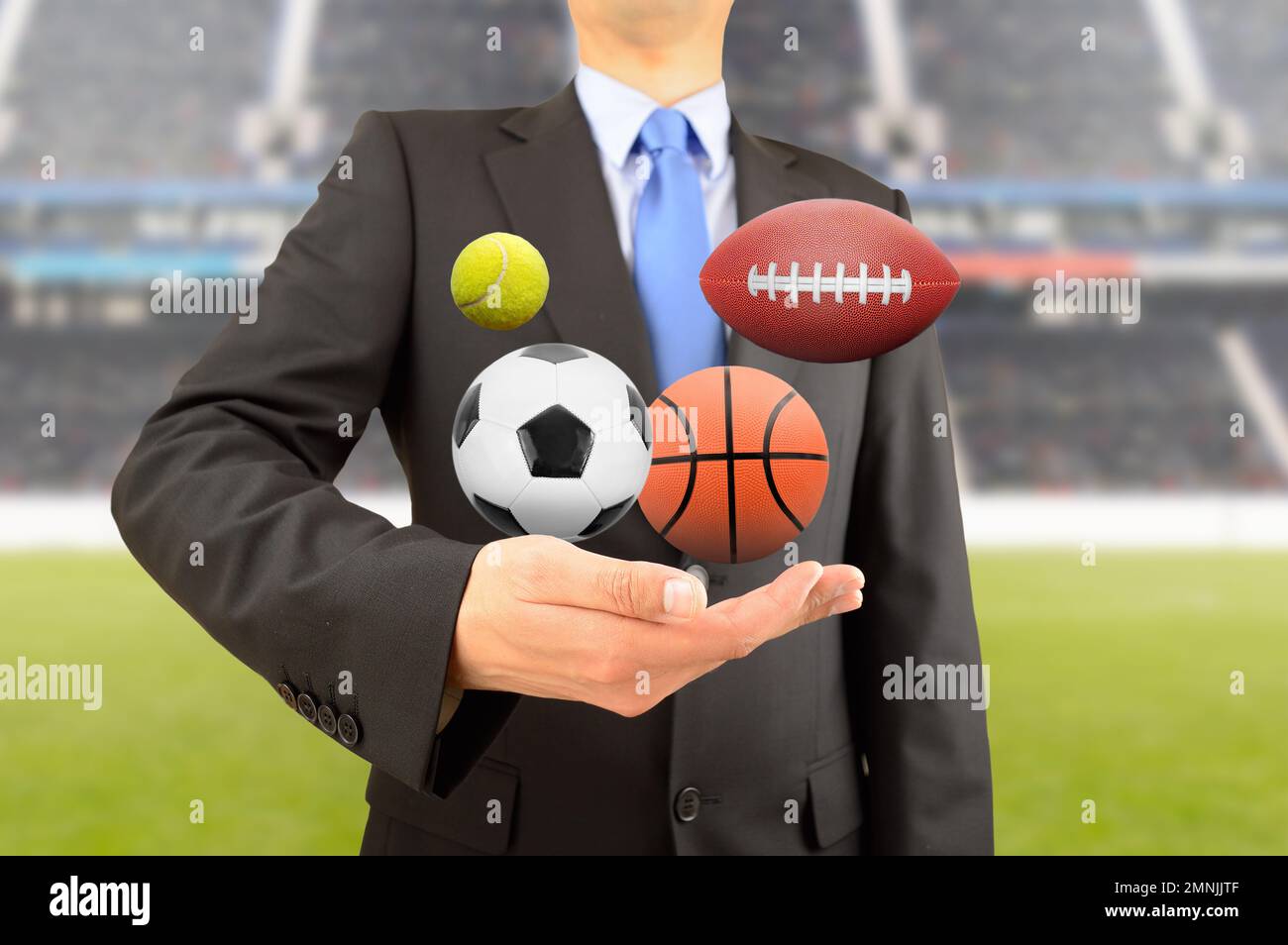 Business man with group of balls of different sports in hand at stadium ...