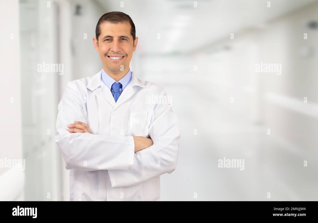 A handsome doctor standing with his arms folded and smiling at the ...