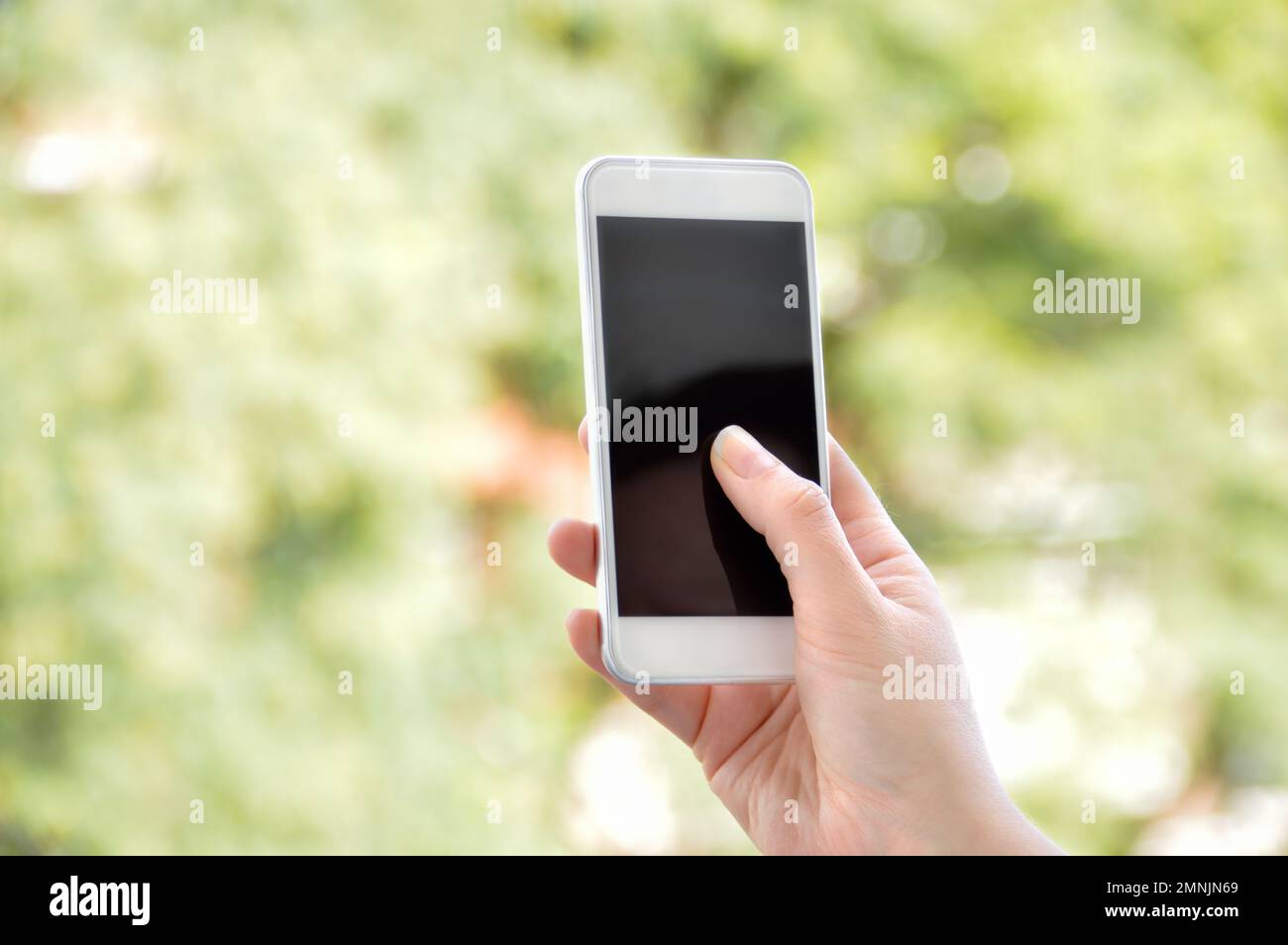 Woman hand holding a smart phone outdoor with a green nature background ...