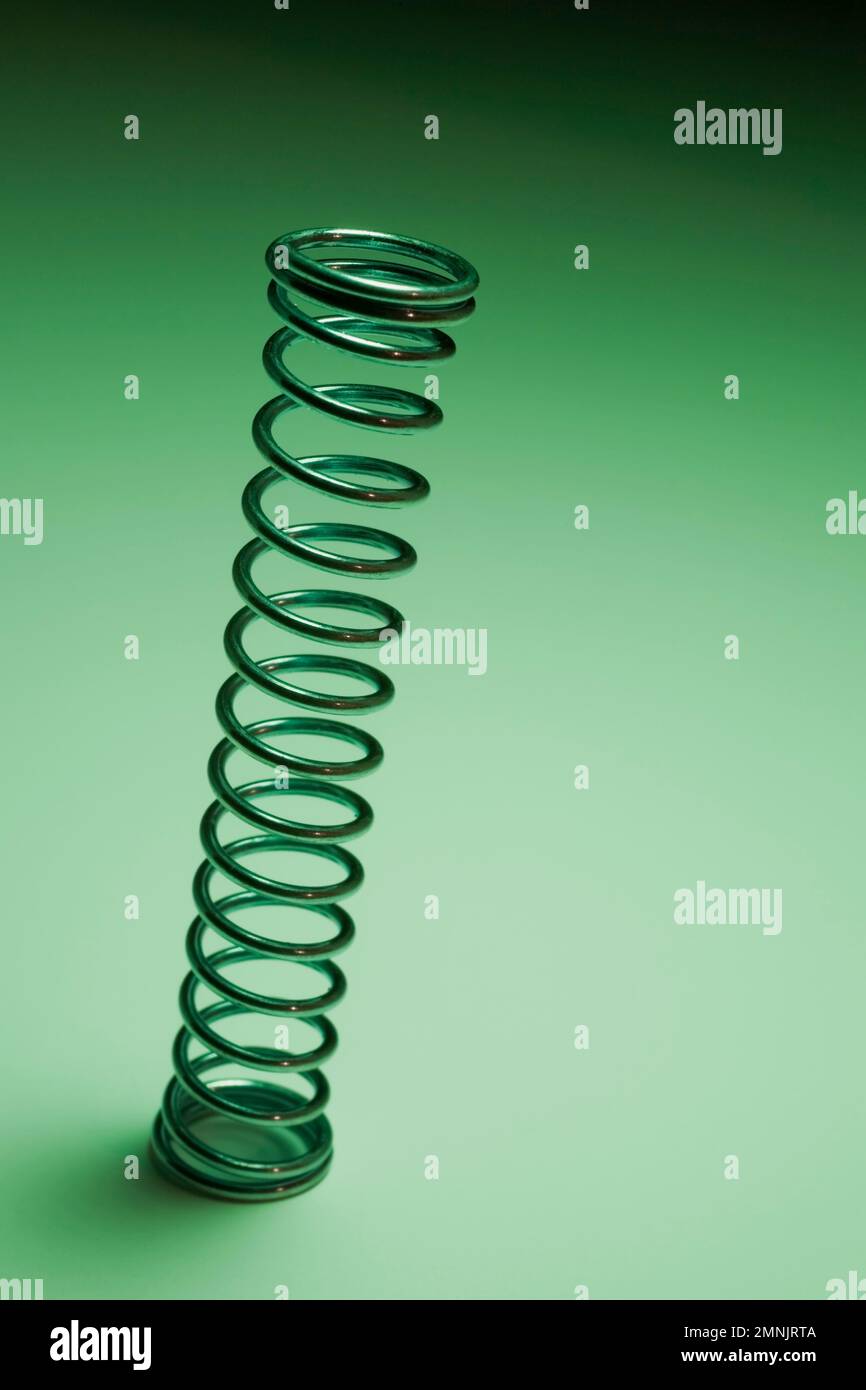 Upright coiled metal spring on green background Stock Photo - Alamy