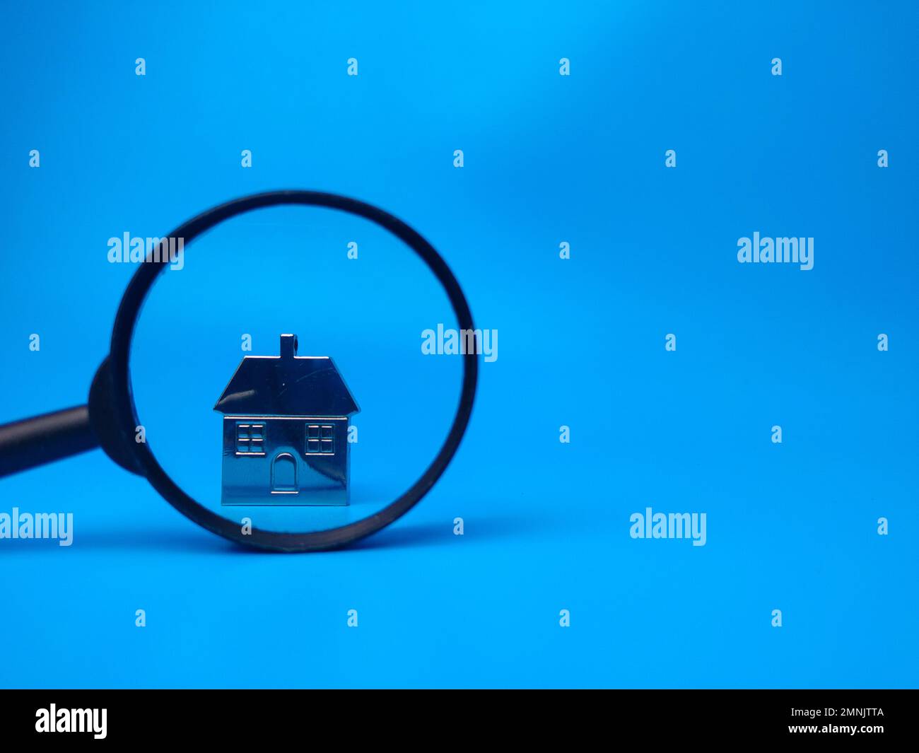 Miniature house and magnifying glass on blue background with copy space ...