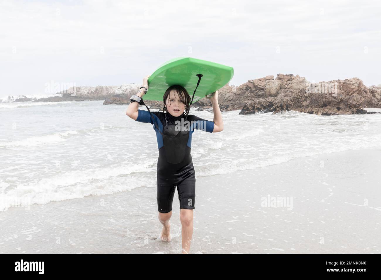 Boy (10-11) carrying bodyboard on Voelklip beach Stock Photo - Alamy