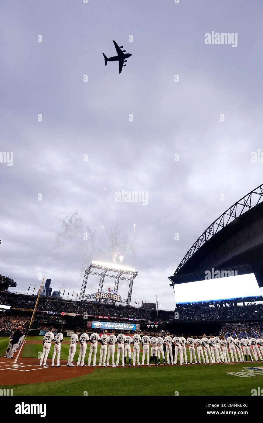 Seattle Mariners players and coaches line the first base line as a C-17 ...