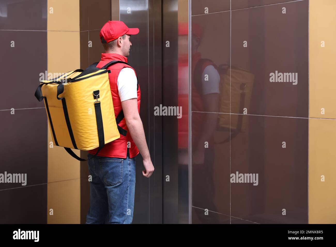 Male courier with thermo bag waiting for elevator. Food delivery ...