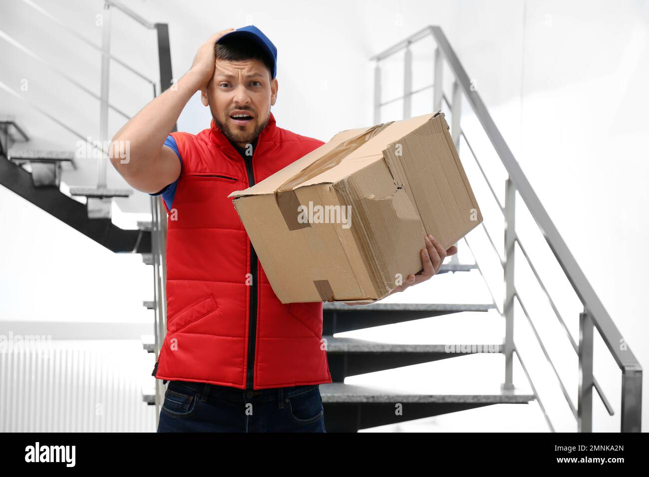 Emotional courier with damaged cardboard box indoors. Poor quality ...