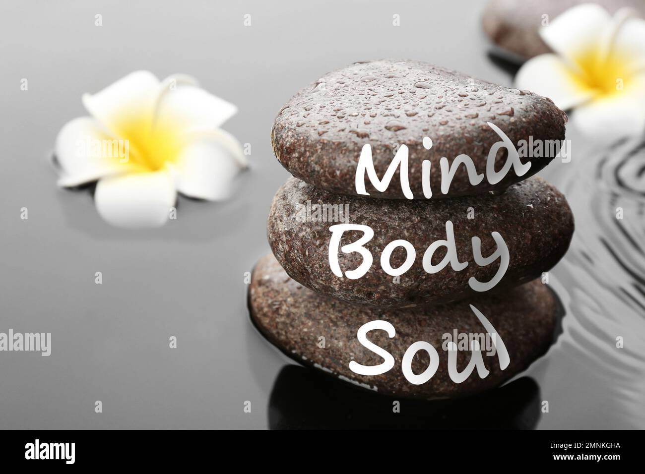 Spa stones with words Mind, Body, Soul and plumeria flowers in water ...