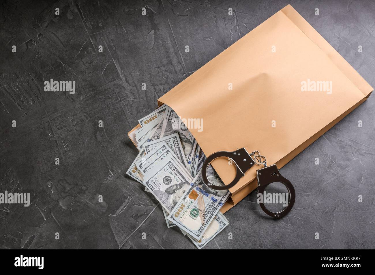 Envelope with dollar bills and handcuffs on grey stone table, top view ...
