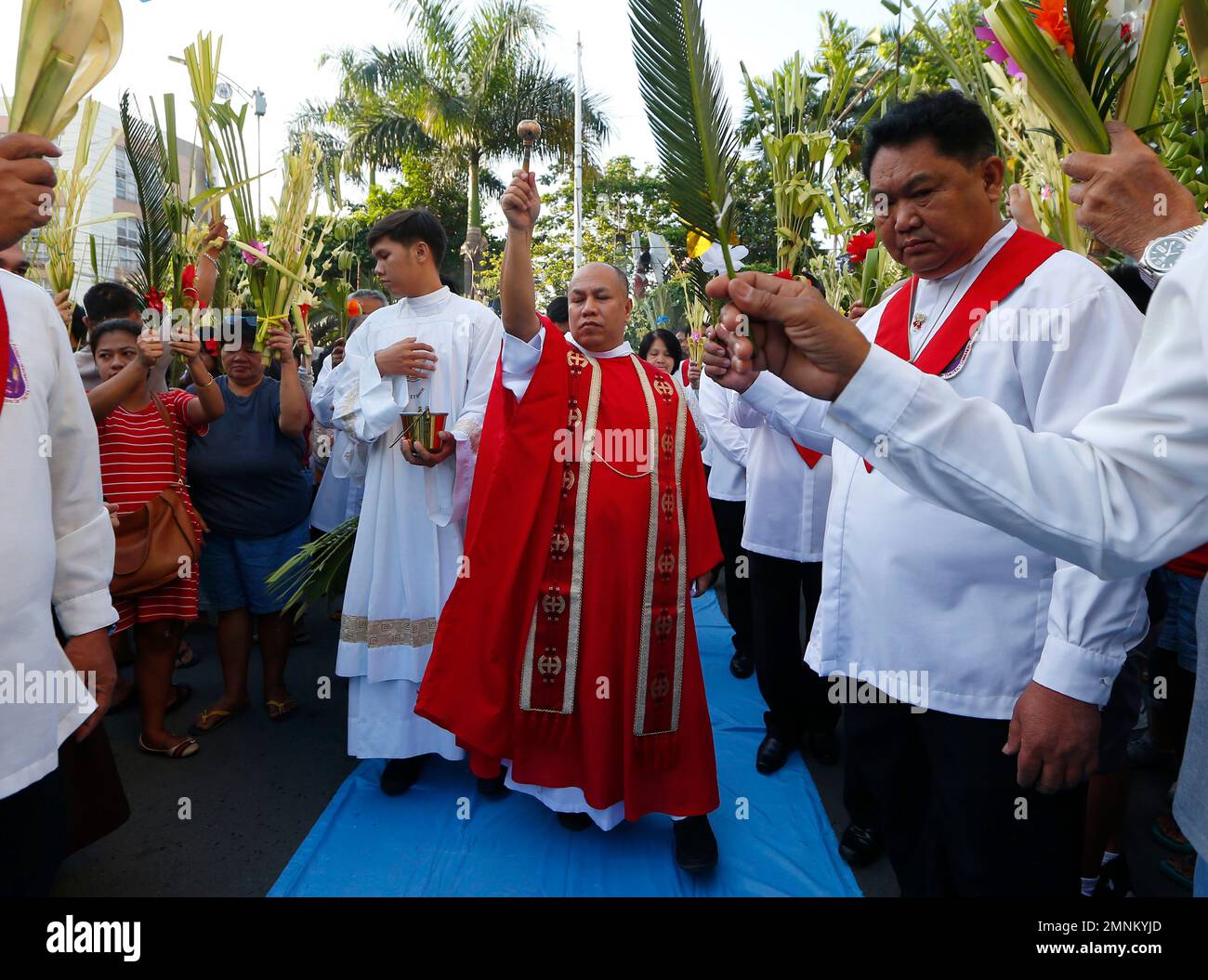 A Roman Catholic priest blesses with holy water palm frond-waving ...