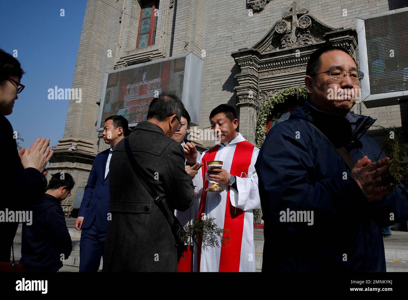 Chinese Catholics line up to receive bread from a priest outside the ...