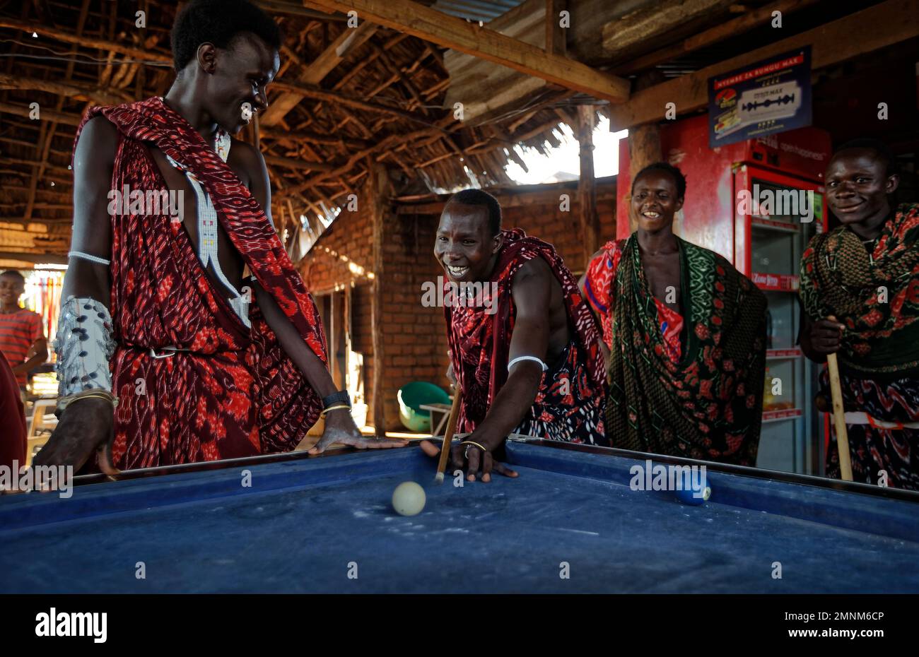 Young Maasai men relax and play a game of pool at a bar by the side of ...