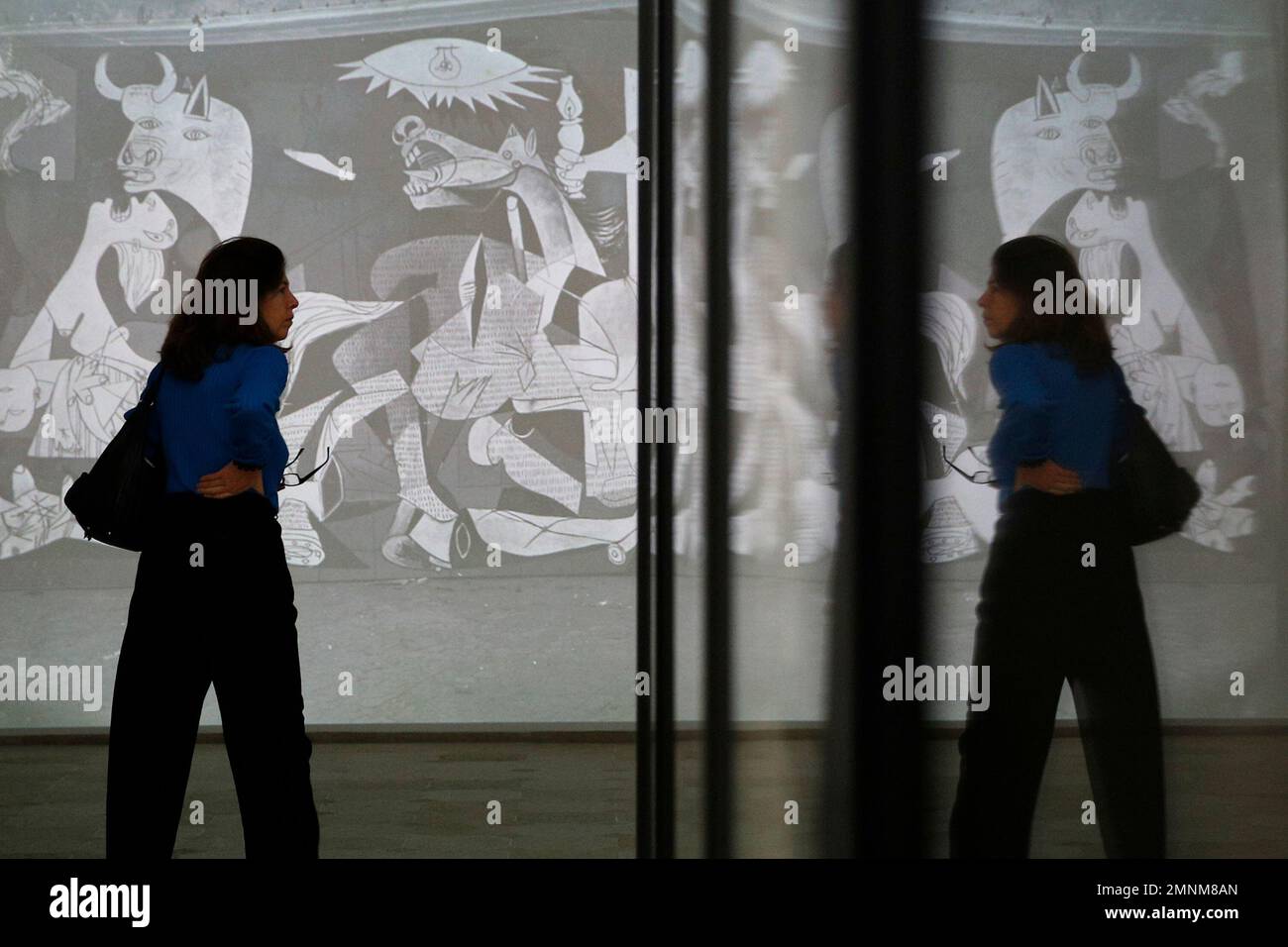 A woman is reflected on " Guernica Redacted (After Picasso's Guernica, 1937)" by Robert Longo as ...