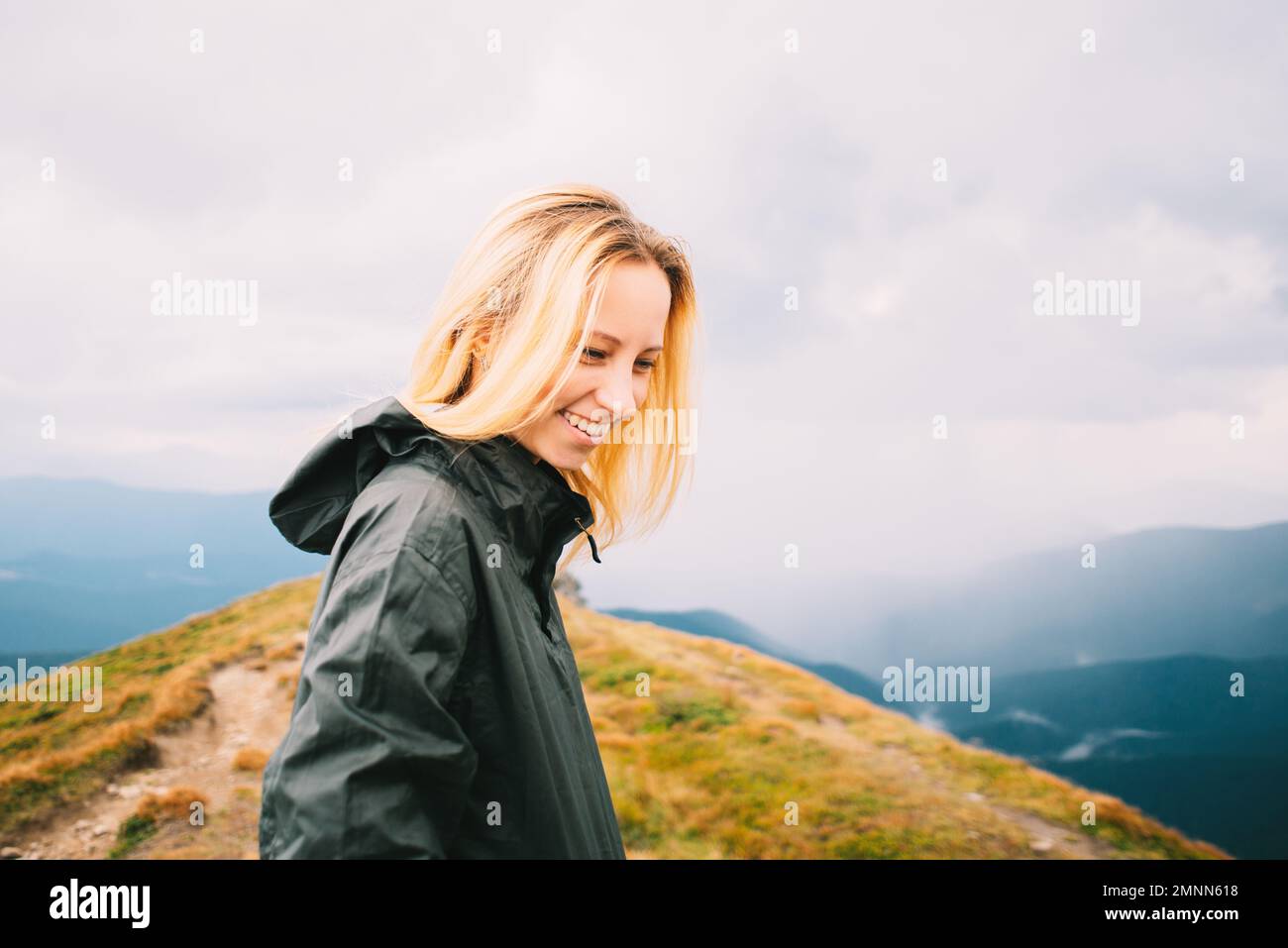 Cute one young blonde female hiker against a backdrop of mountain range ...