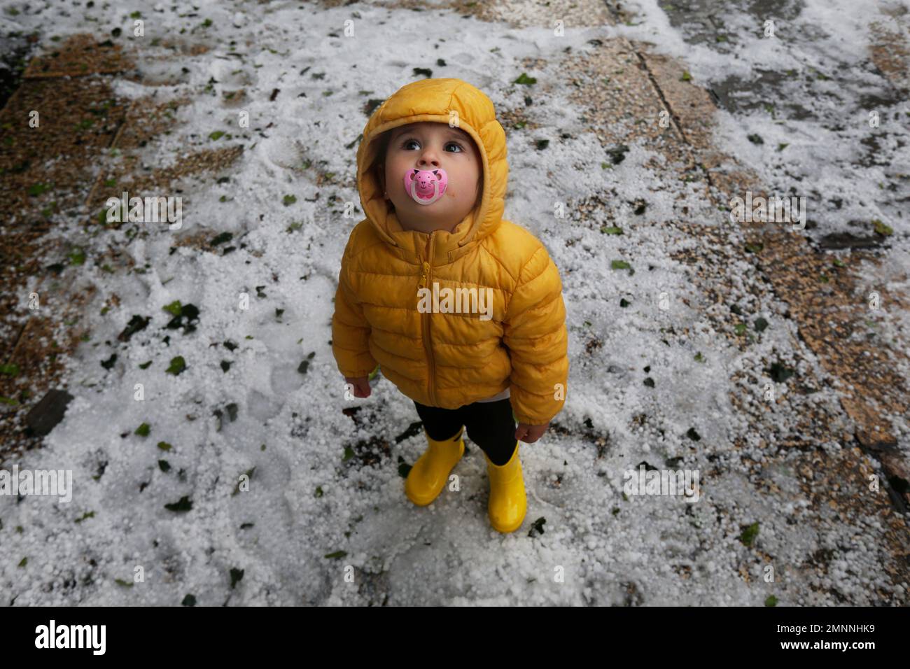 A child stands over a sidewalk covered in hail after a violent rain ...