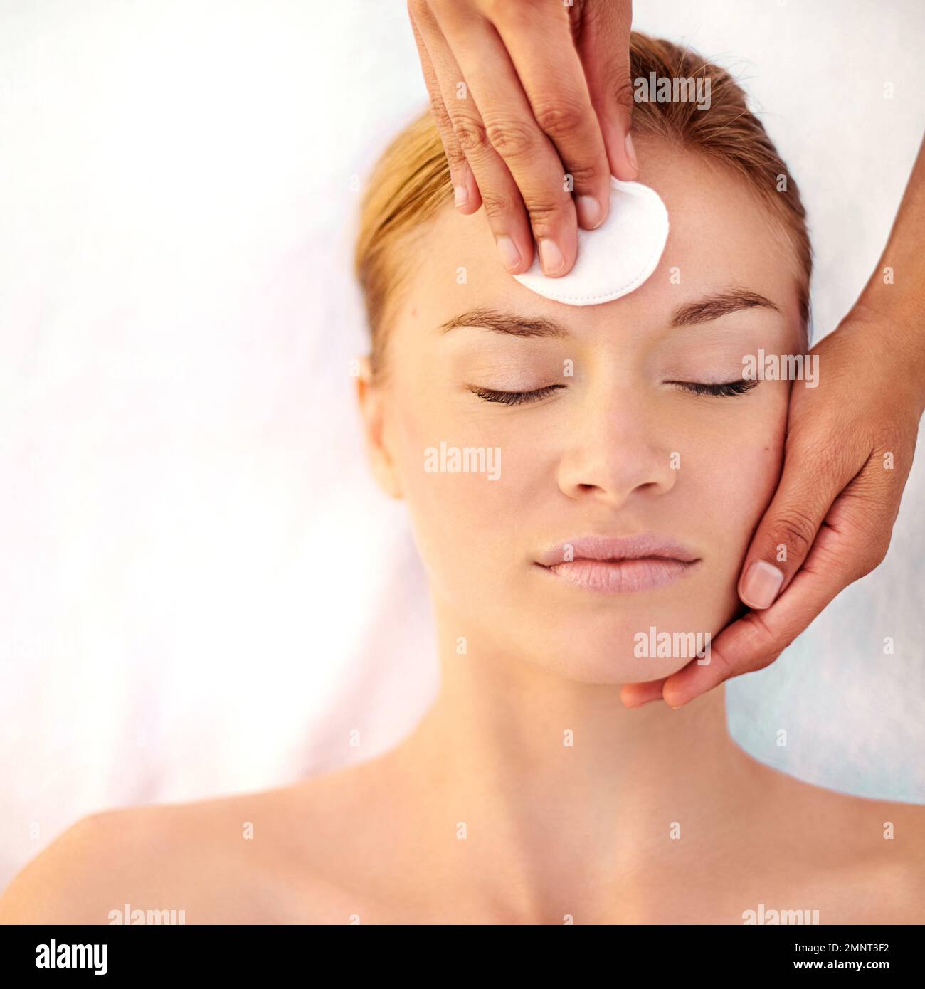 Applying a gentle cleanser to her skin. a young woman getting a facial ...