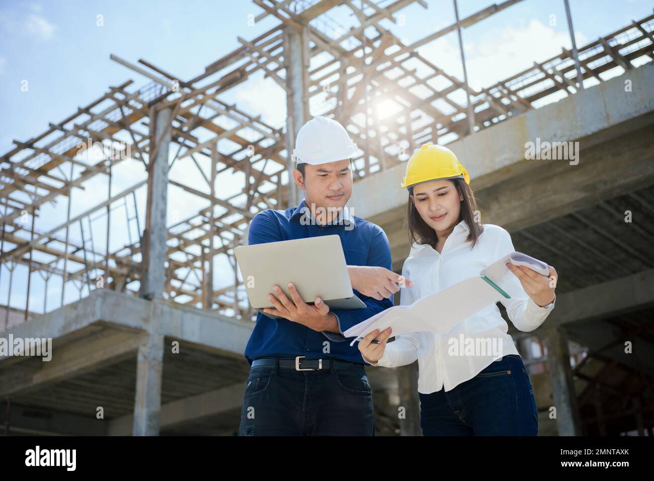 Asian Architector and engineers team with draft plan of building and tablet talking constructing ...