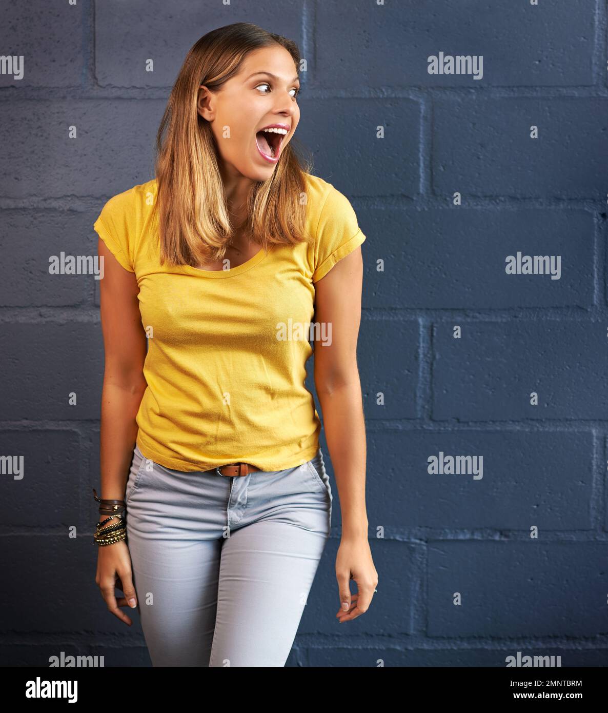 What the...a young woman looking amazed against a brick wall background ...