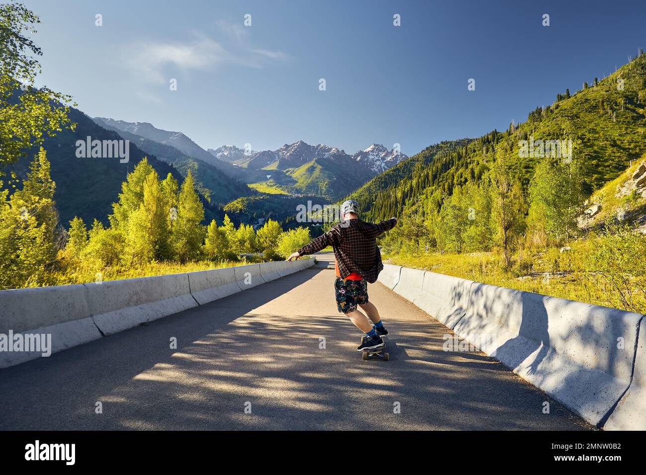 Man Skater in the helmet and orange shirt ride on the mountain road at ...