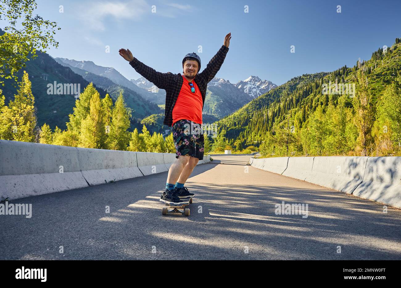 Man Skater in the helmet and orange shirt ride on the mountain road at ...