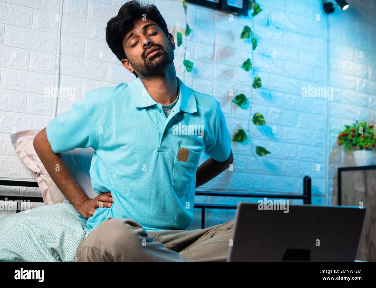 young man suffering back pain while working in laptop on bed at night ...