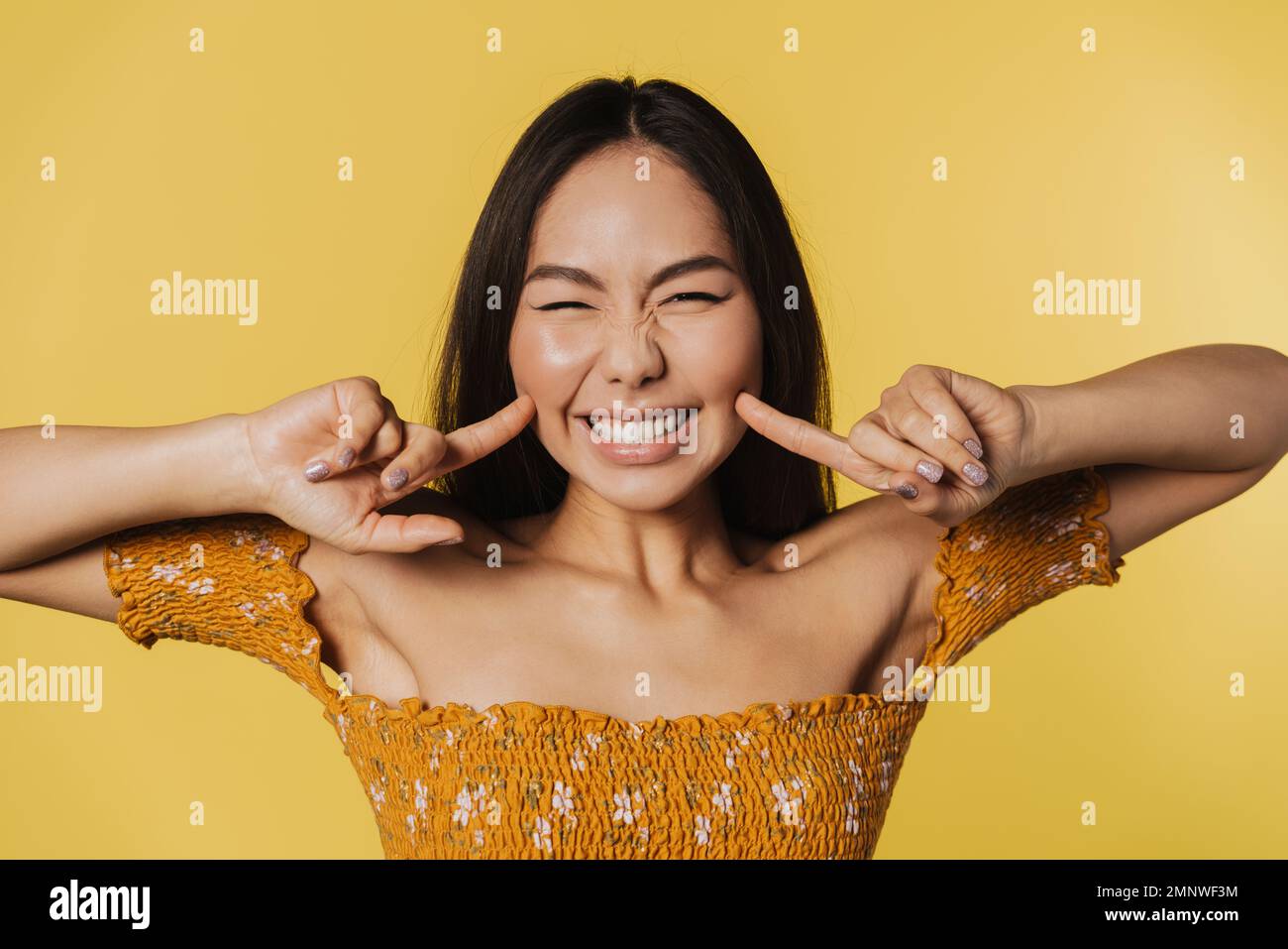 Young asian woman smiling while pointing fingers at her cheeks isolated ...