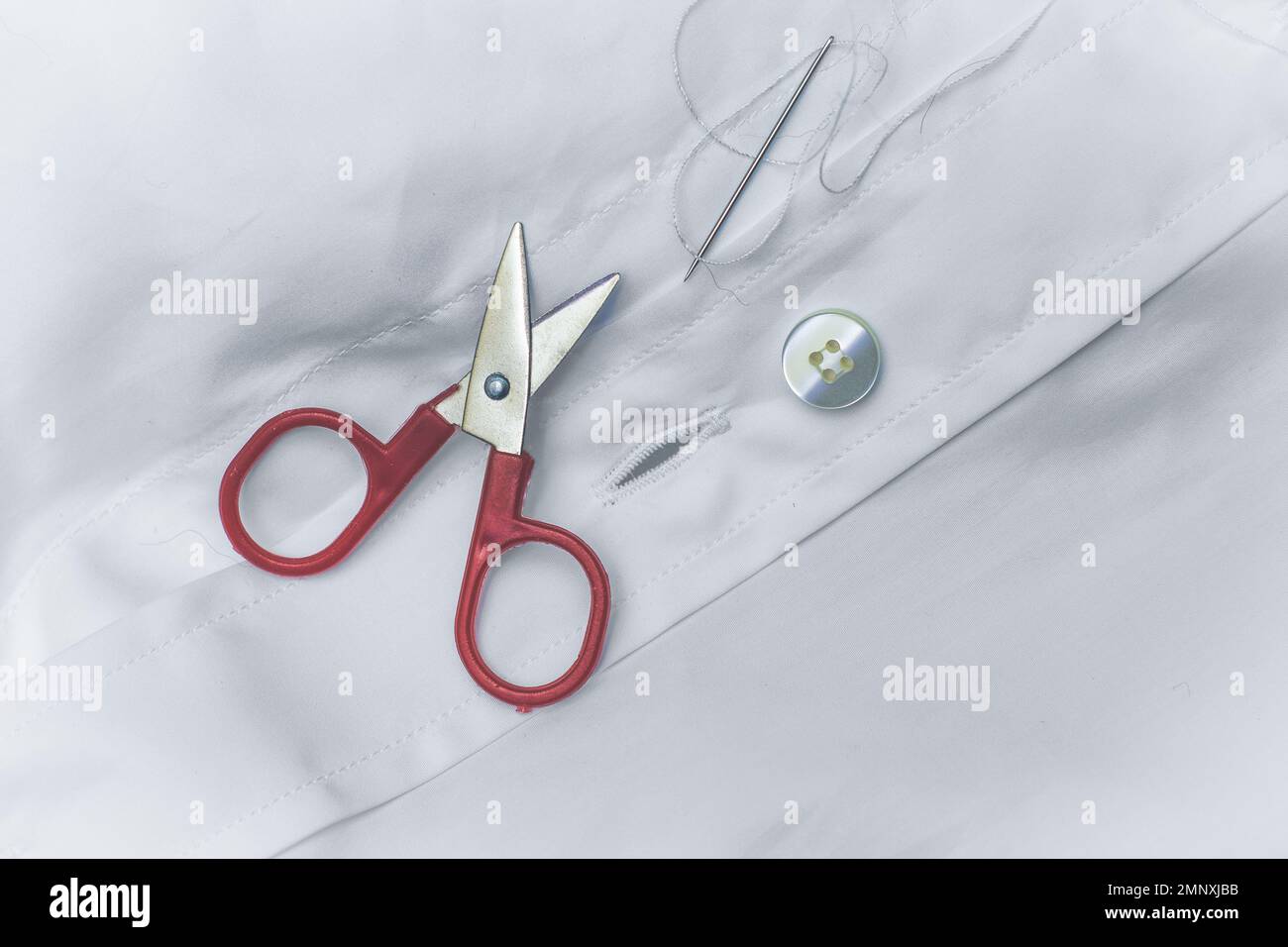 Sewing needle and thread drills to mend a broken button on shirt Stock ...