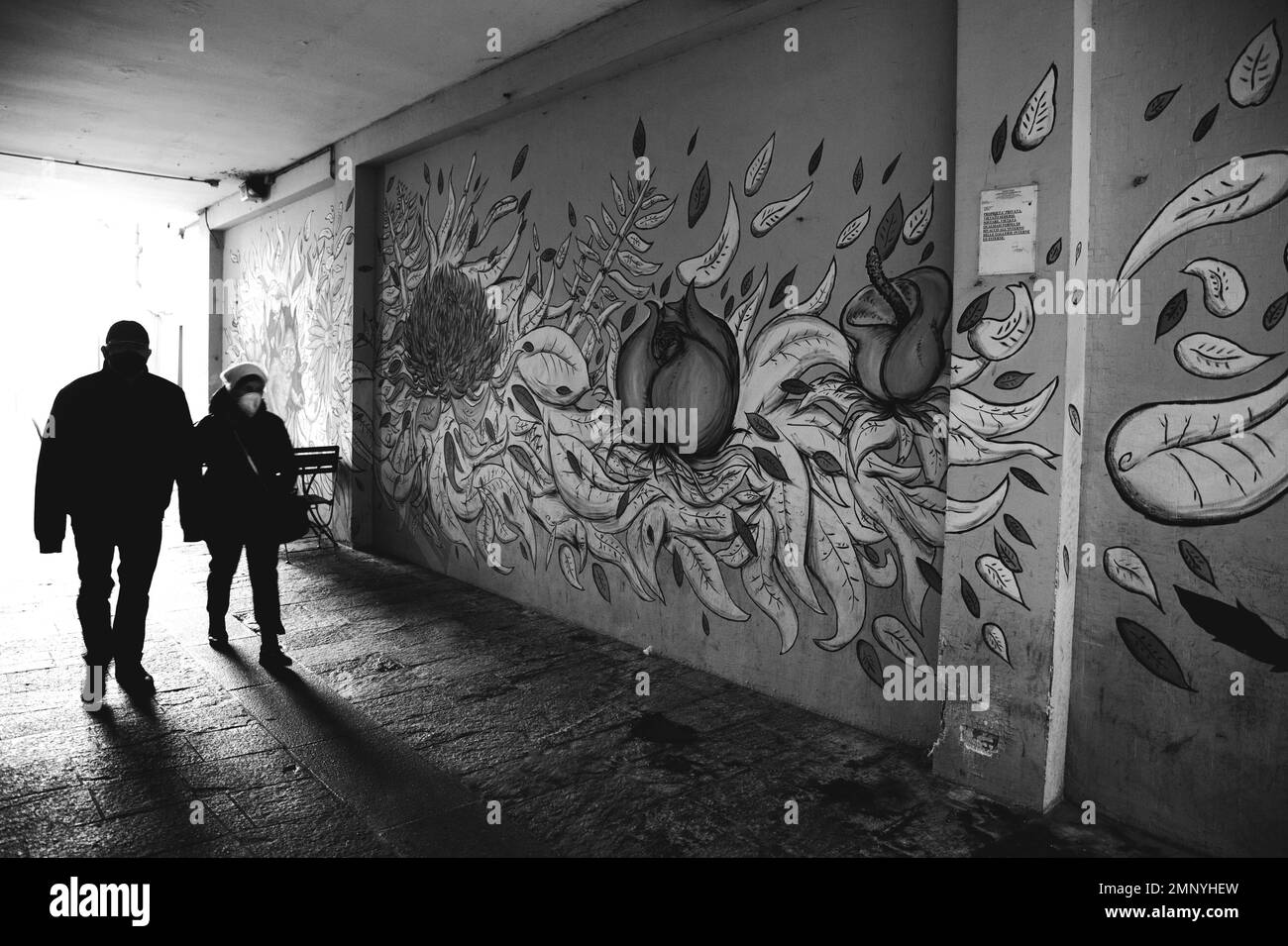 two people walk past a wall with murals Stock Photo - Alamy