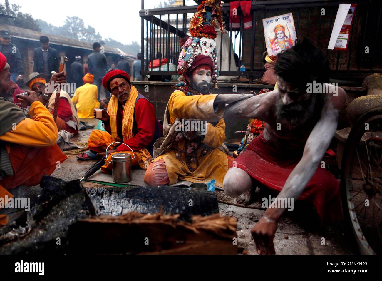 A Hindu holy man helps another to smear his body with ash and vermilion ...