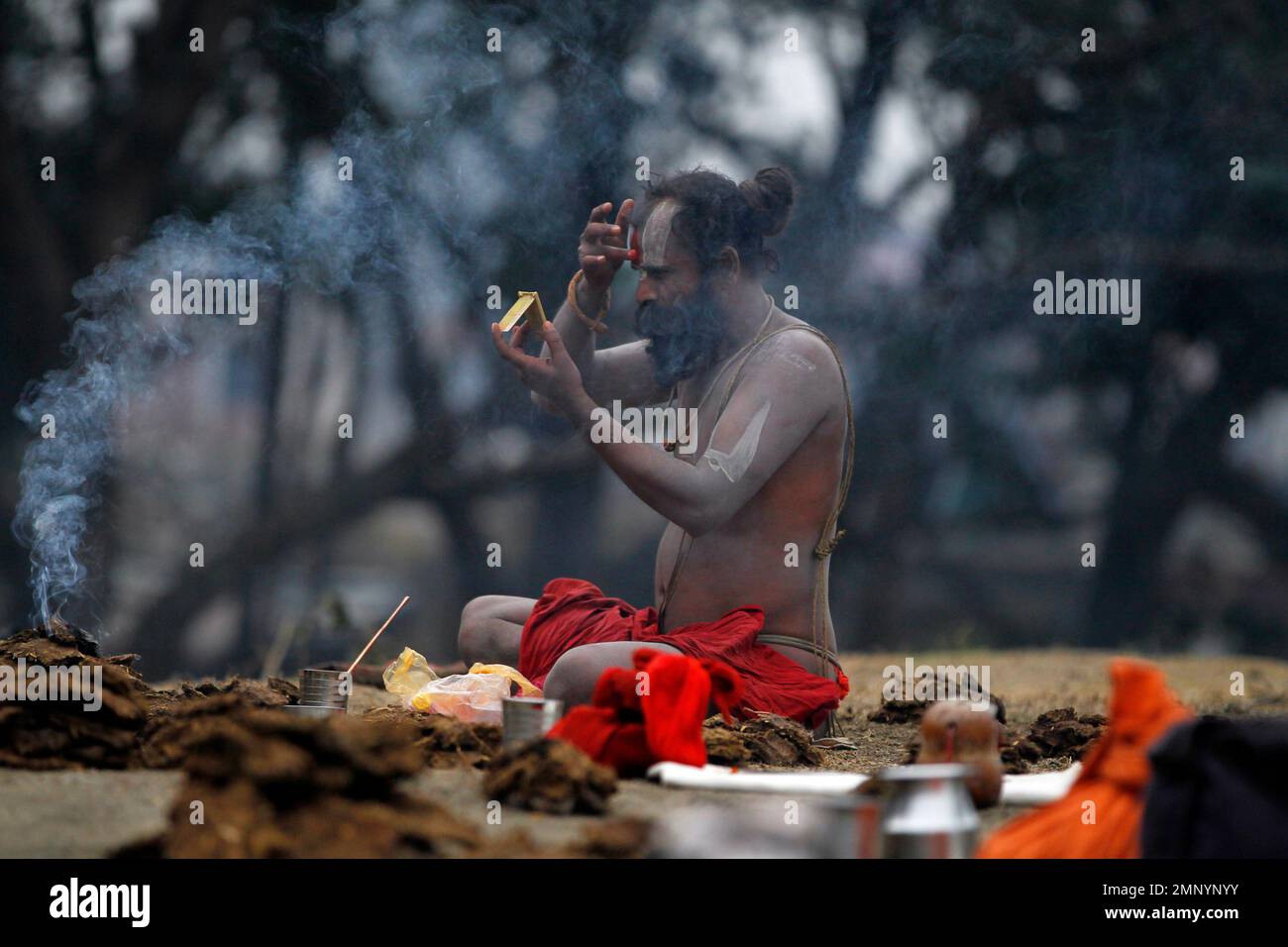 A Hindu holy man smears vermilion powder on his face at the courtyard ...