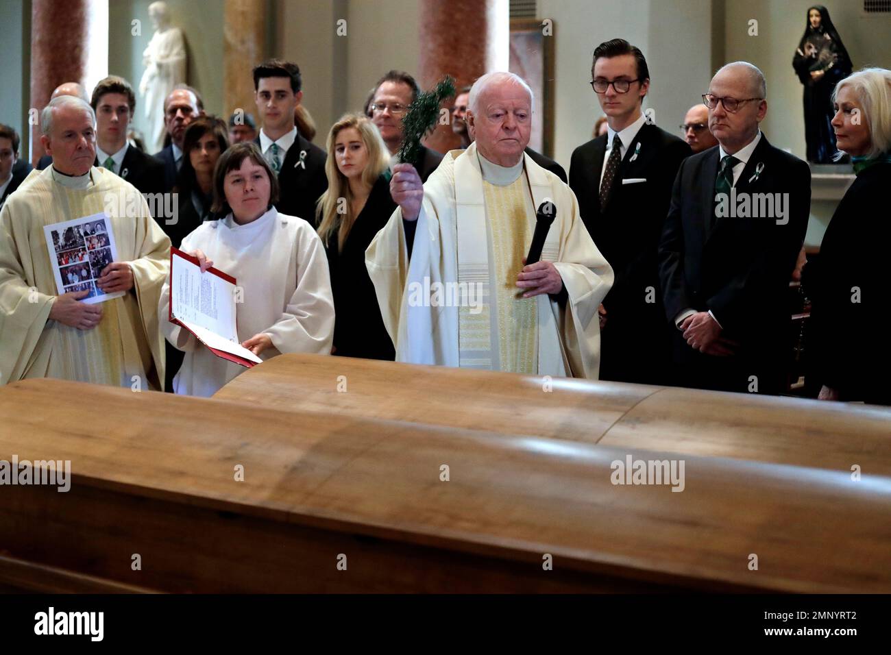 As family members look on, the Rev. Oliver Duggan sprinkles holy water ...