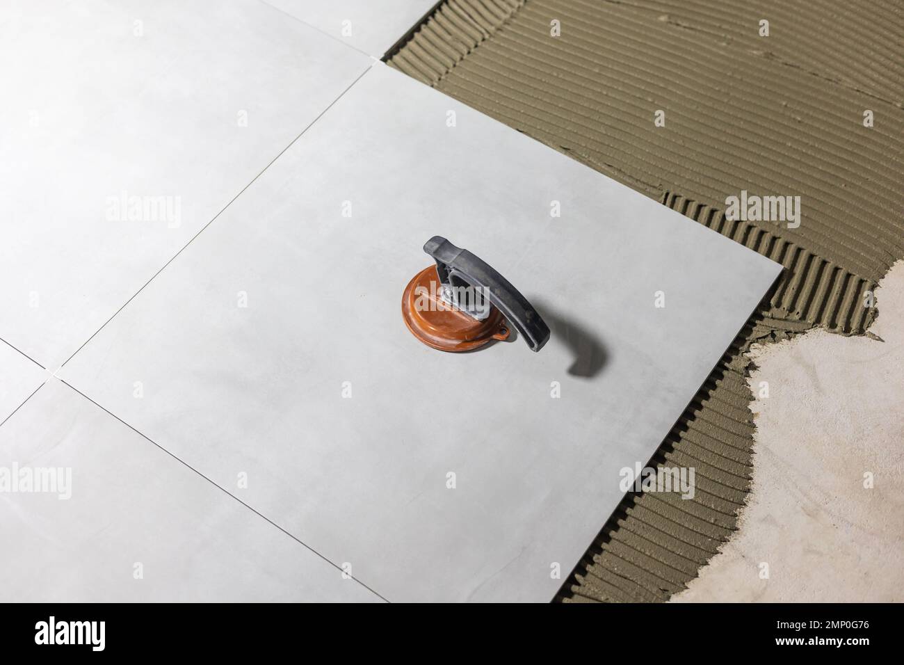 Tiler worker placing or tiling gray ceramic tile in the position over ...