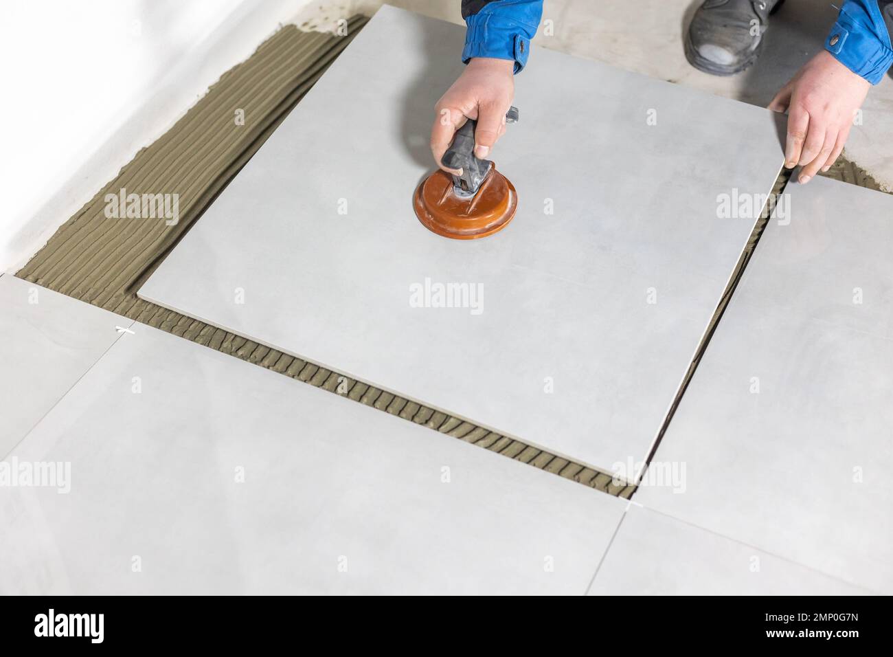 Tiler worker placing or tiling gray ceramic tile in the position over ...