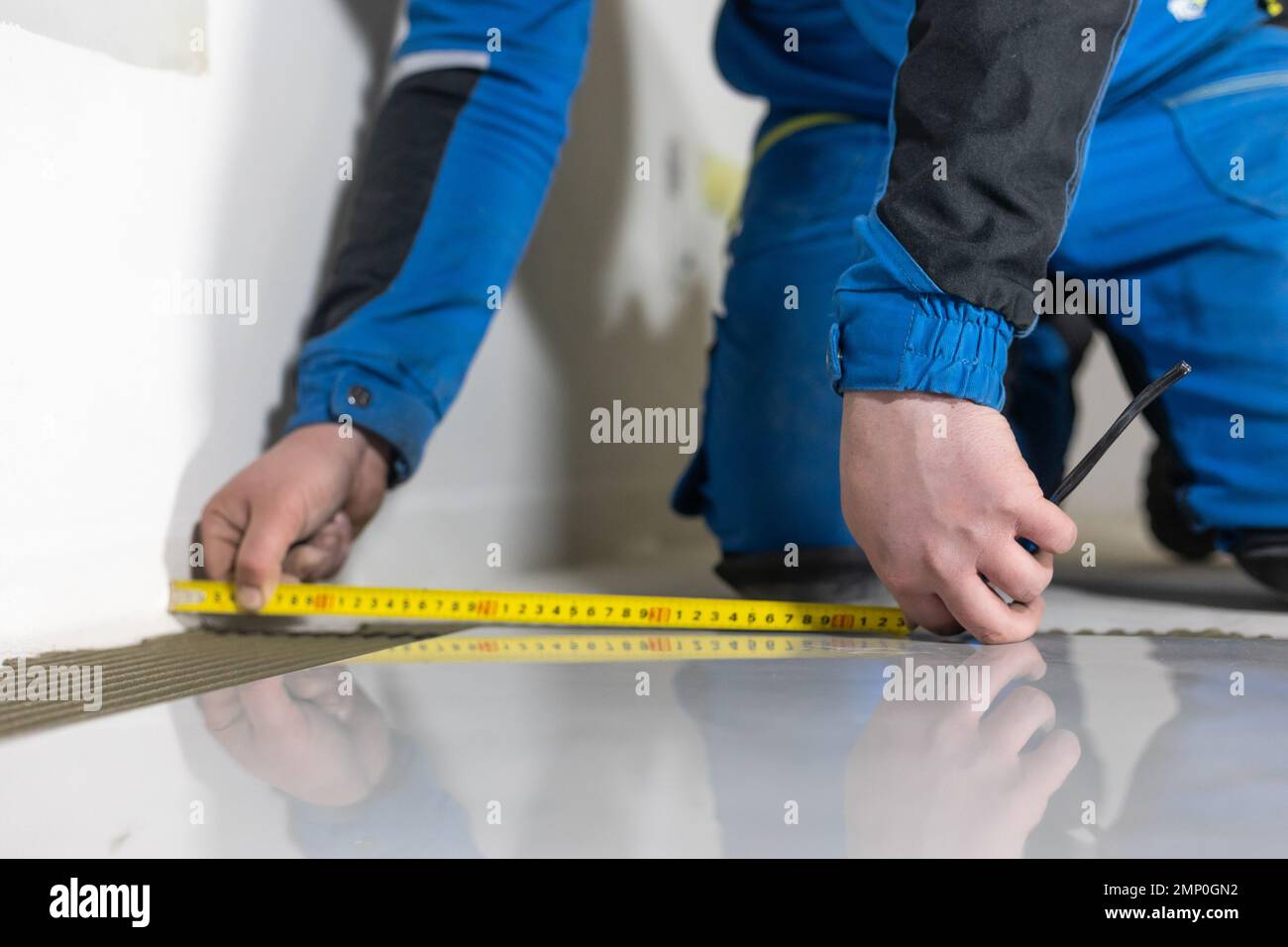 Tiler worker placing or tiling gray ceramic tile in the position over ...