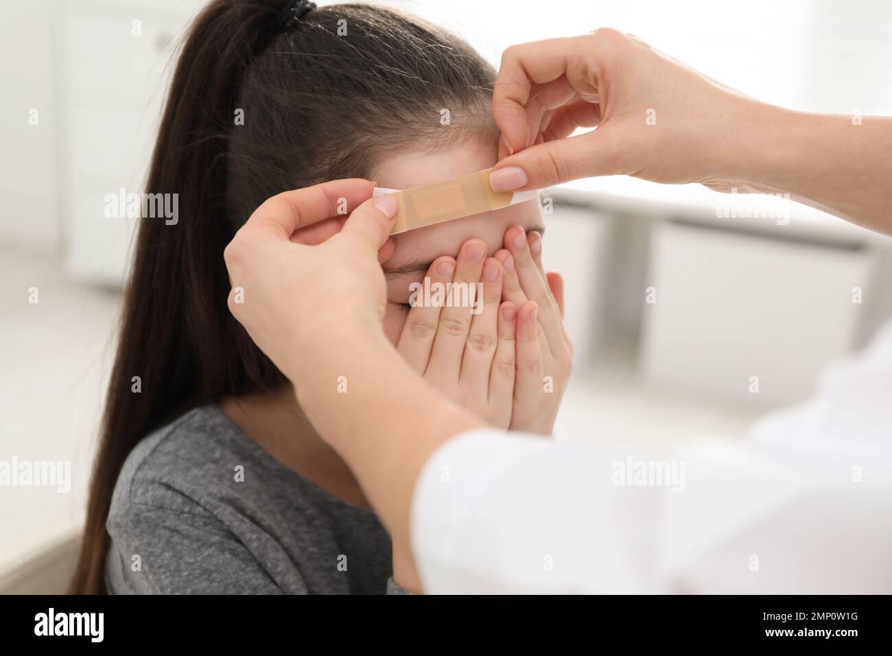 Doctor putting sticking plaster onto girl's forehead indoors Stock ...