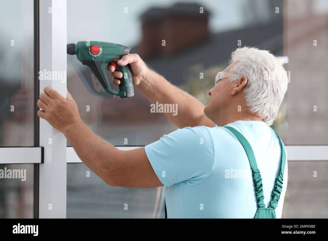 Mature construction worker repairing plastic window with electric ...