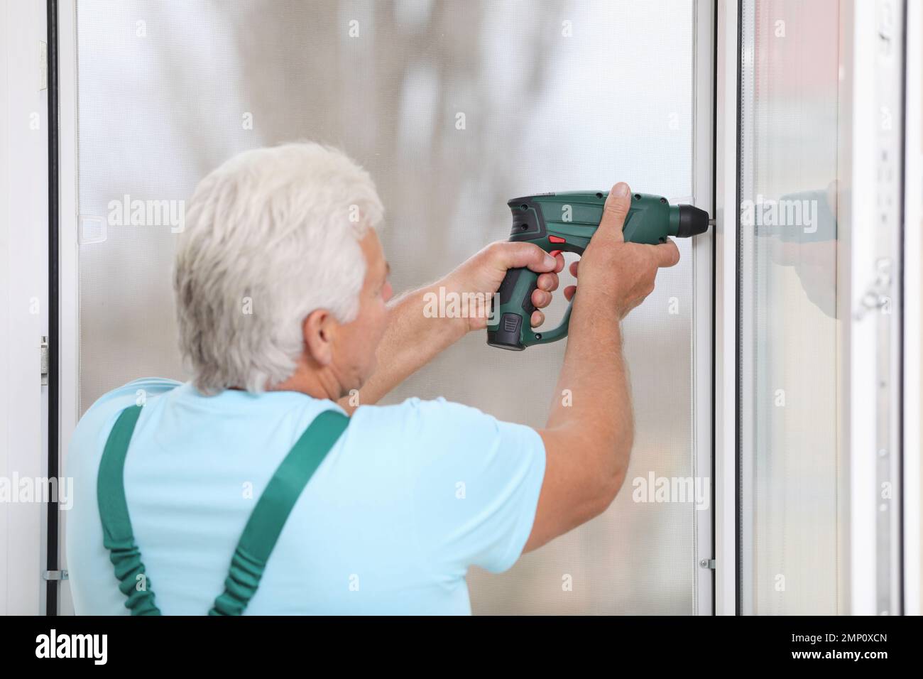 Mature construction worker repairing plastic window with electric ...