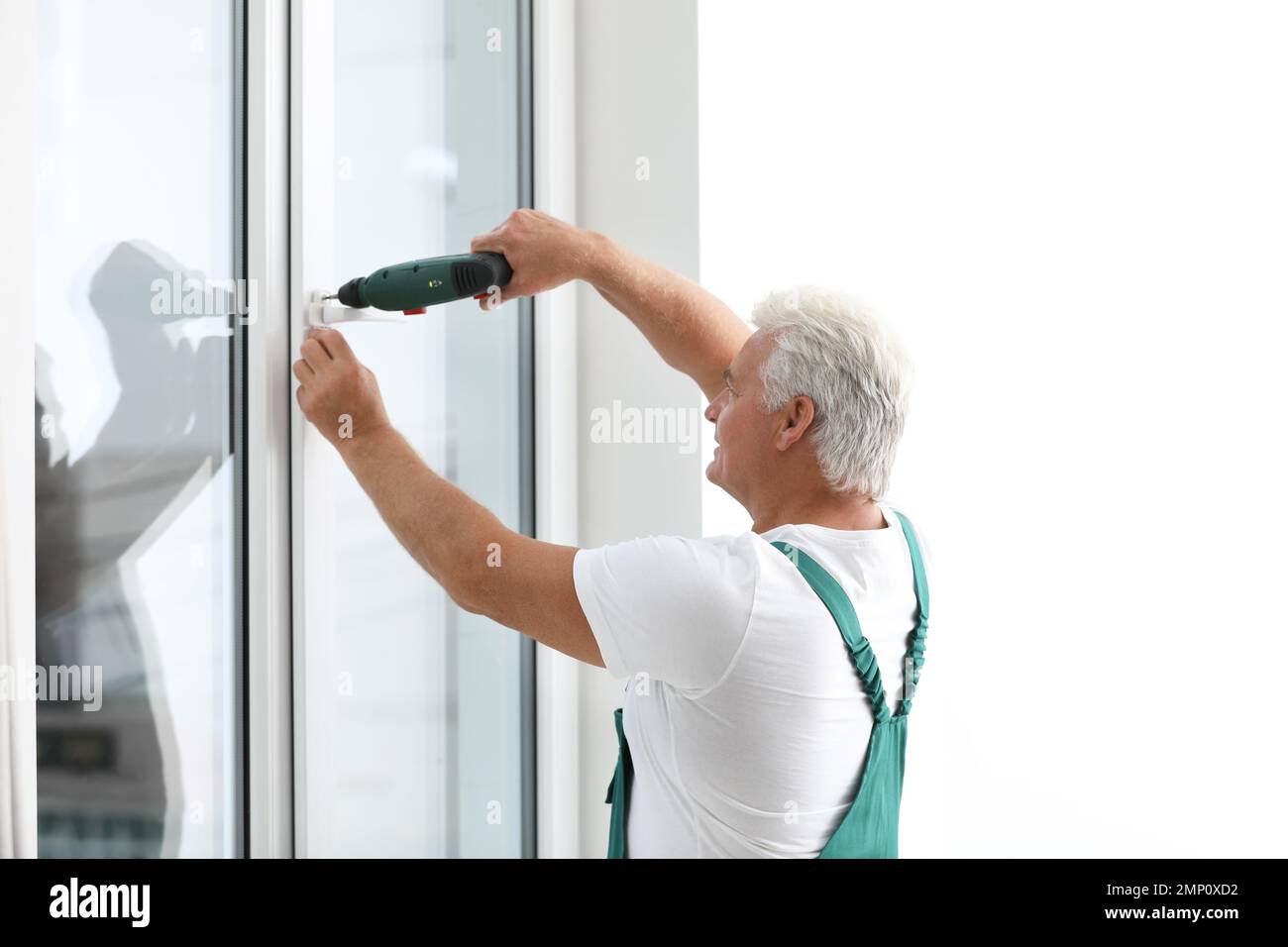 Mature construction worker repairing plastic window with electric ...