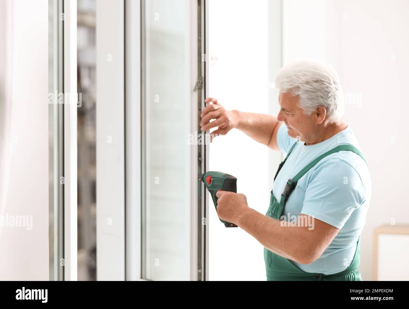 Mature construction worker repairing plastic window with electric ...