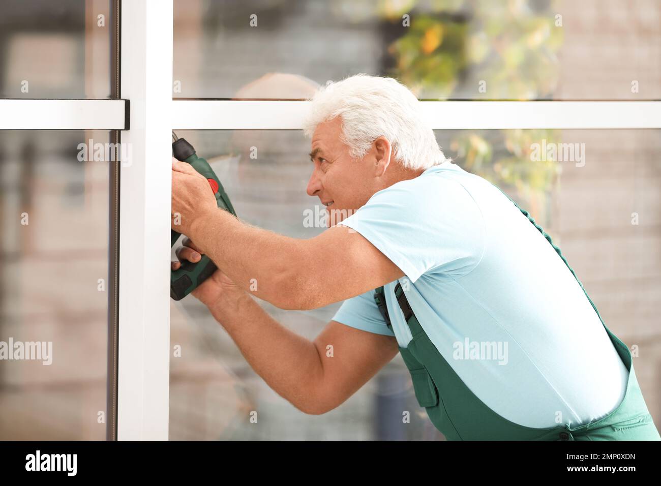 Mature construction worker repairing plastic window with electric ...