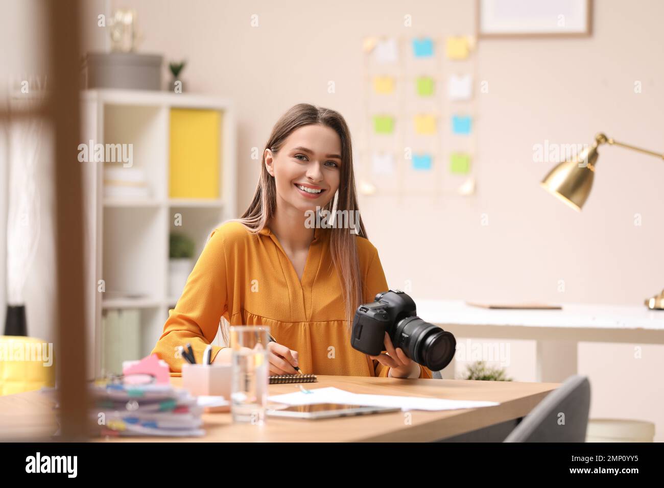Young journalist with camera at table in office Stock Photo - Alamy