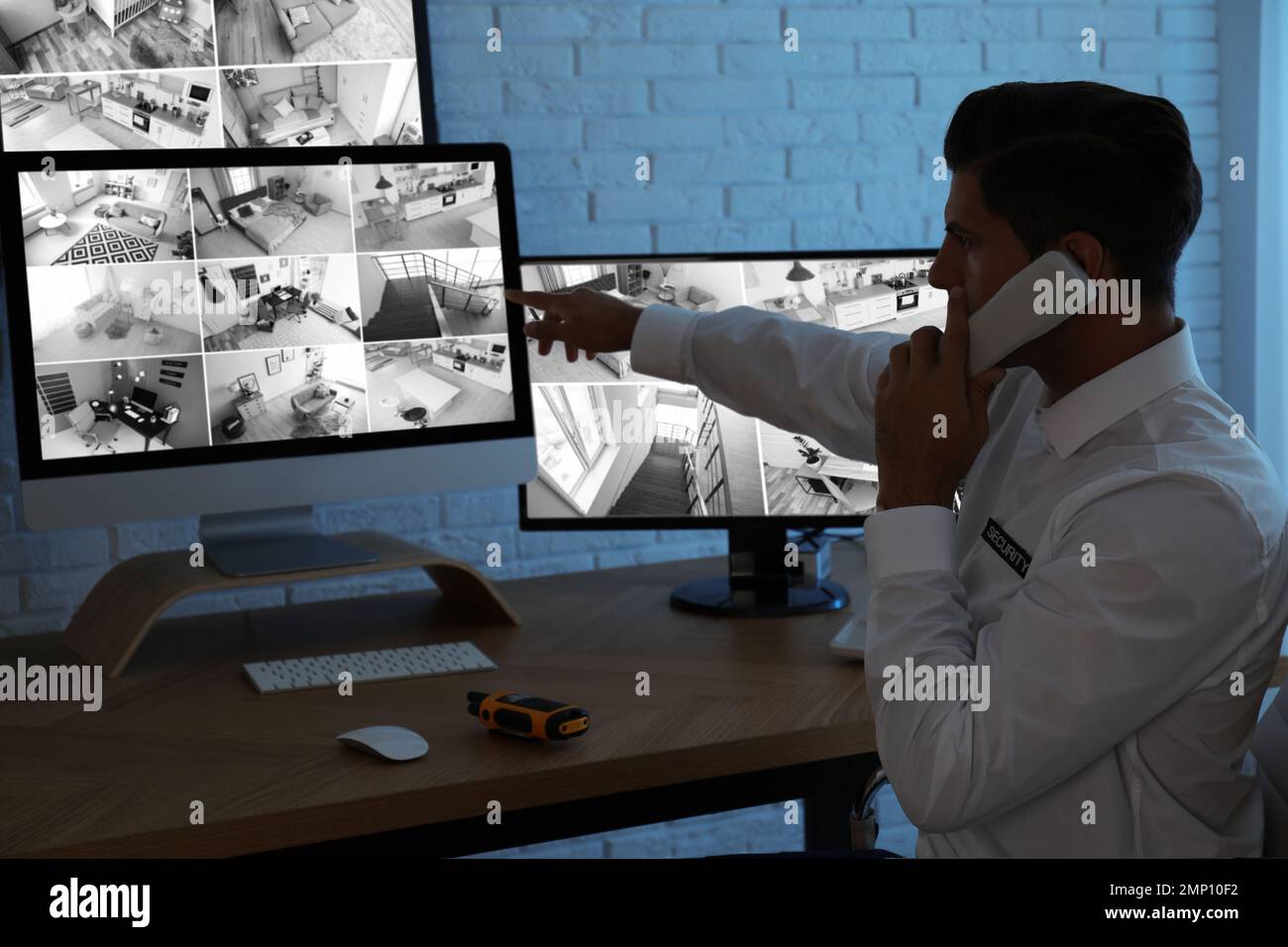 Male security guard talking by telephone near monitors at workplace ...