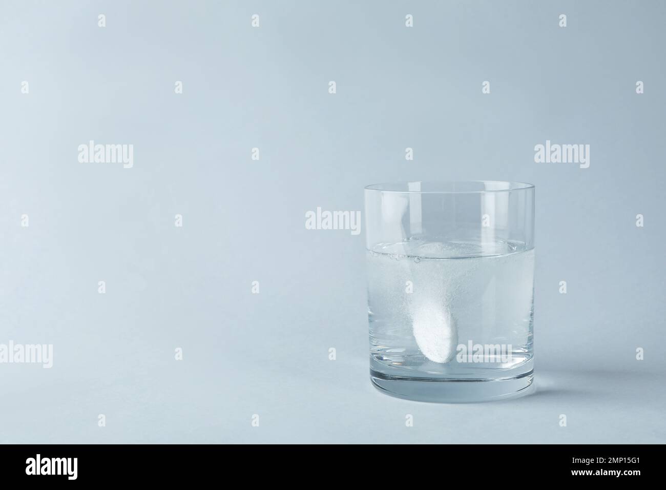 Glass of water with effervescent tablet on light grey background, space ...