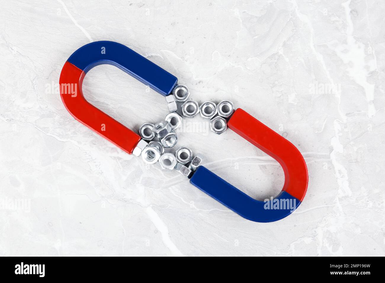 Magnets attracting metal nuts on grey marble table, flat lay Stock ...
