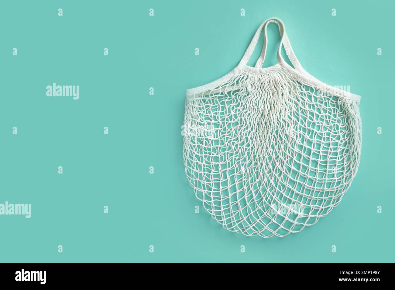 Empty white net bag on turquoise background, top view. Space for text ...