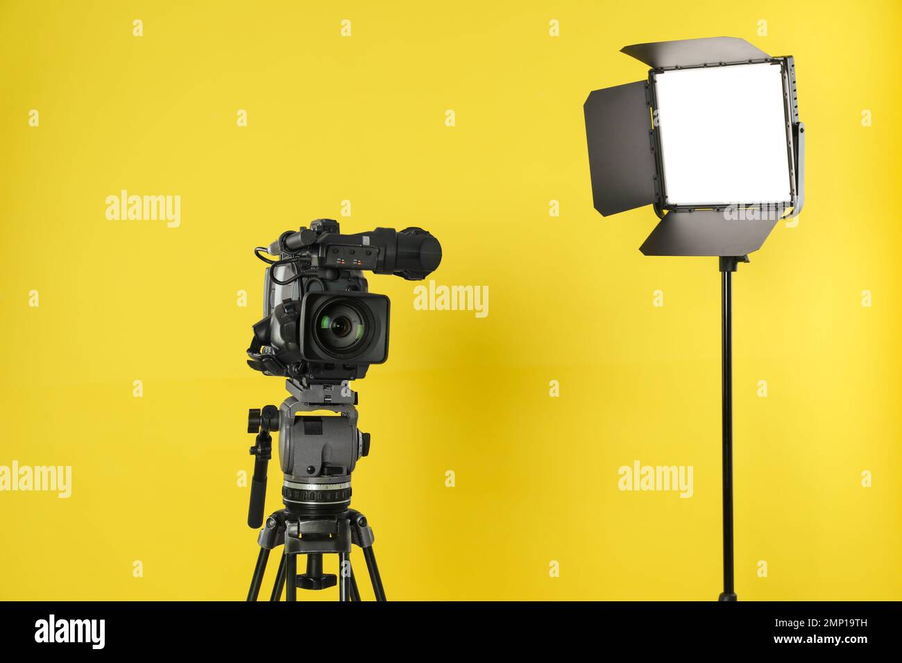 Professional video camera and lighting equipment on yellow background ...