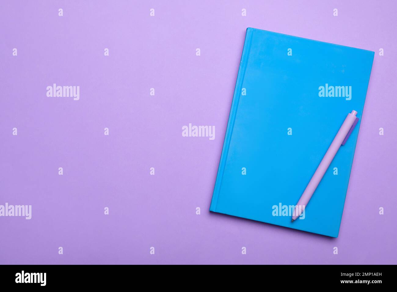 Light blue notebook and pen on lilac background, top view. Space for ...