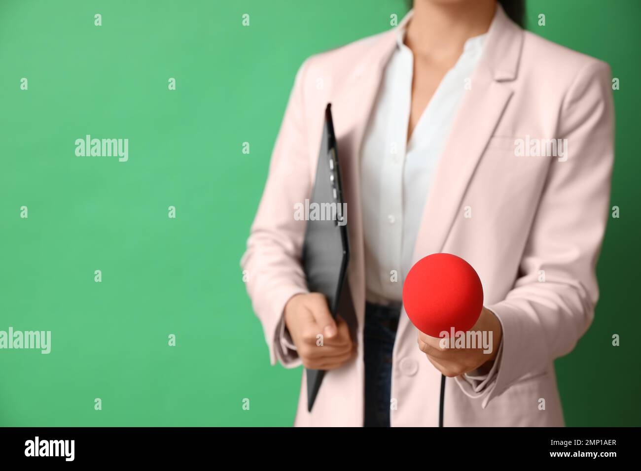 Journalist with microphone and clipboard on green background, closeup ...