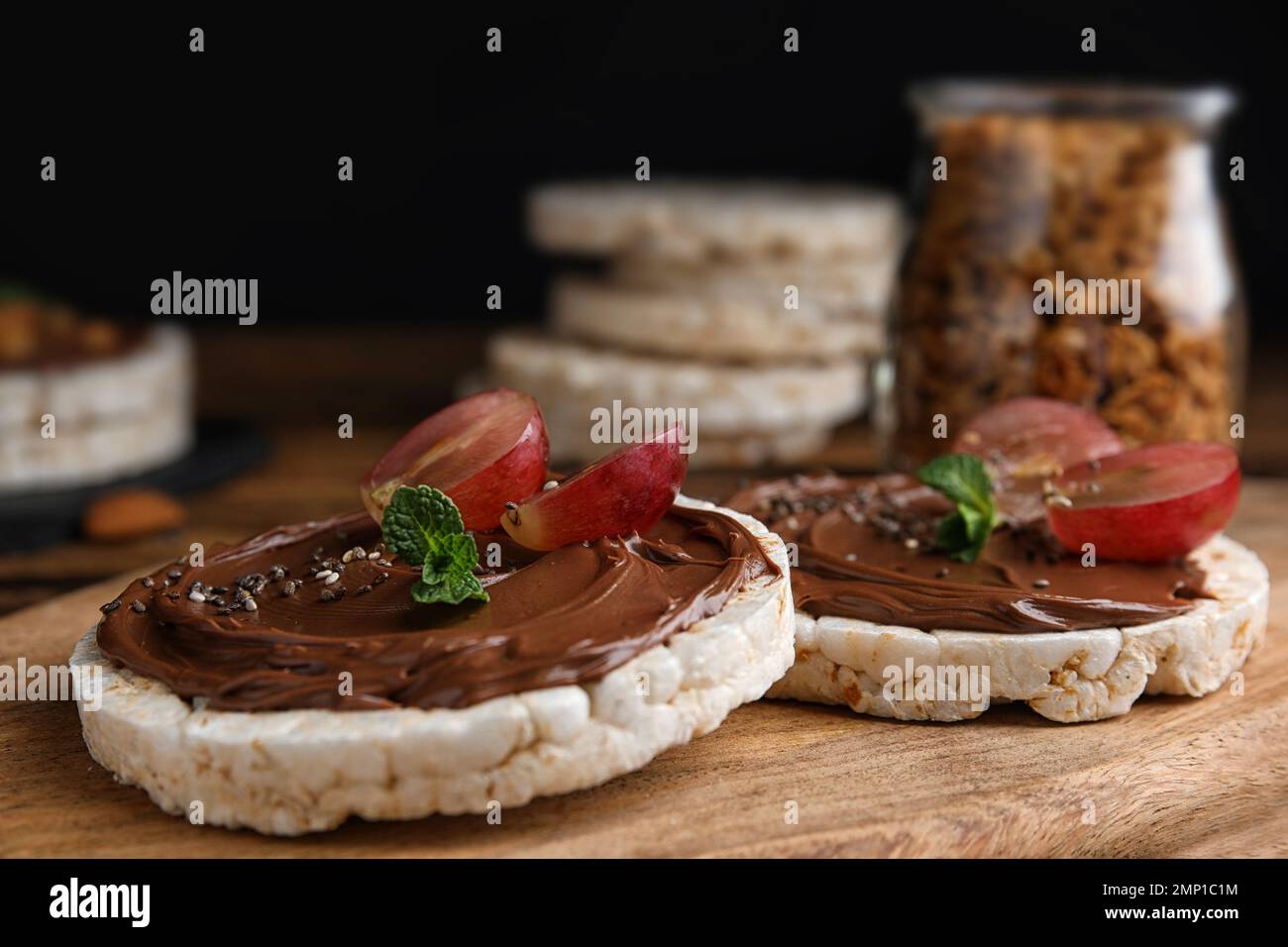 Puffed rice cakes with chocolate spread and grape on wooden board ...