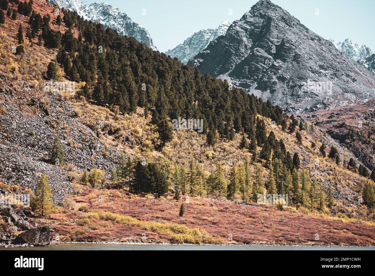 A sharp peak of a triangular stone mountain on another slope with trees ...