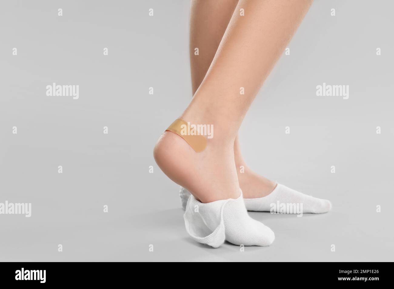 Girl showing foot with sticking plaster on light grey background ...