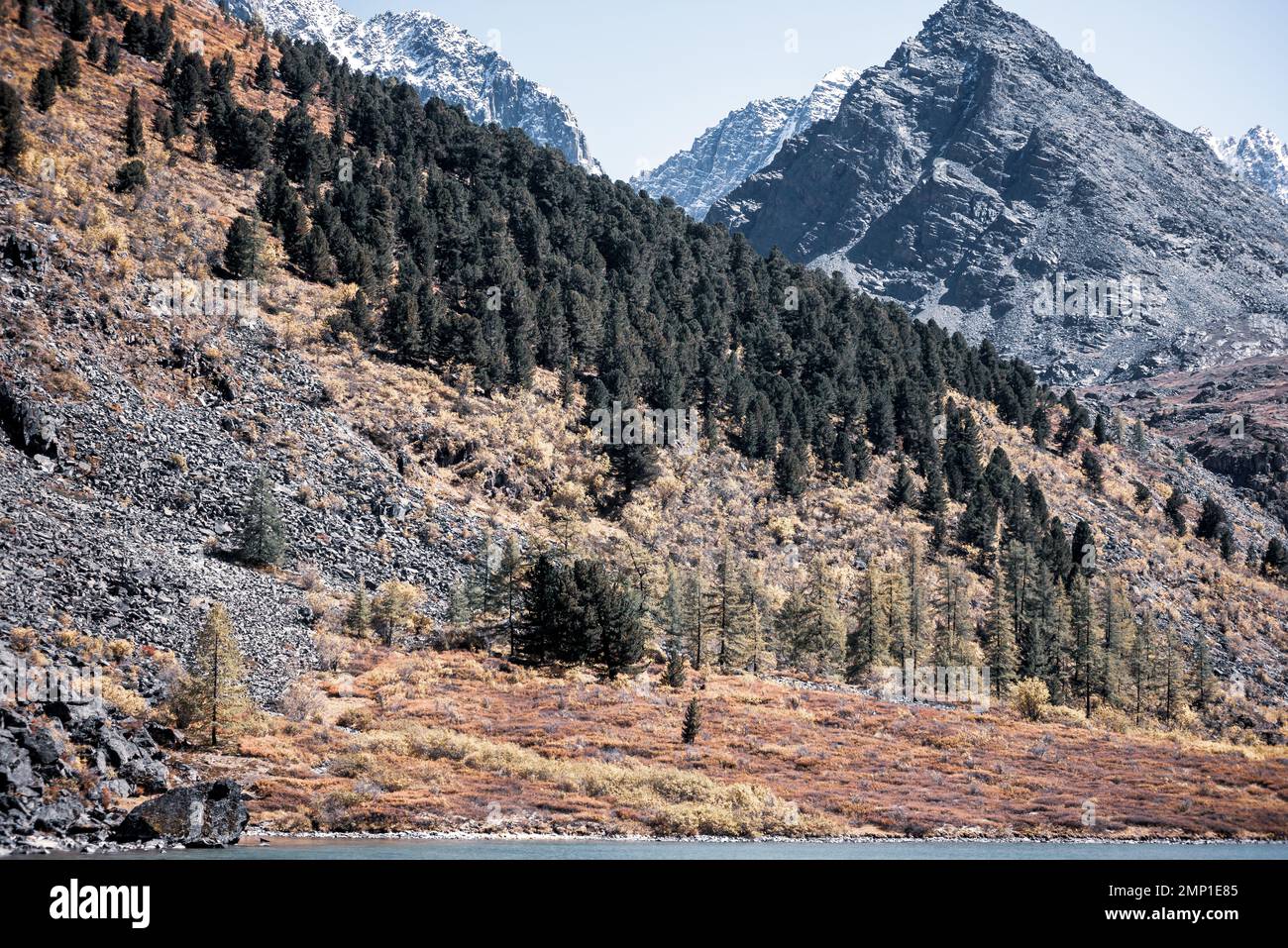 A sharp peak of a triangular stone mountain on another slope with trees ...